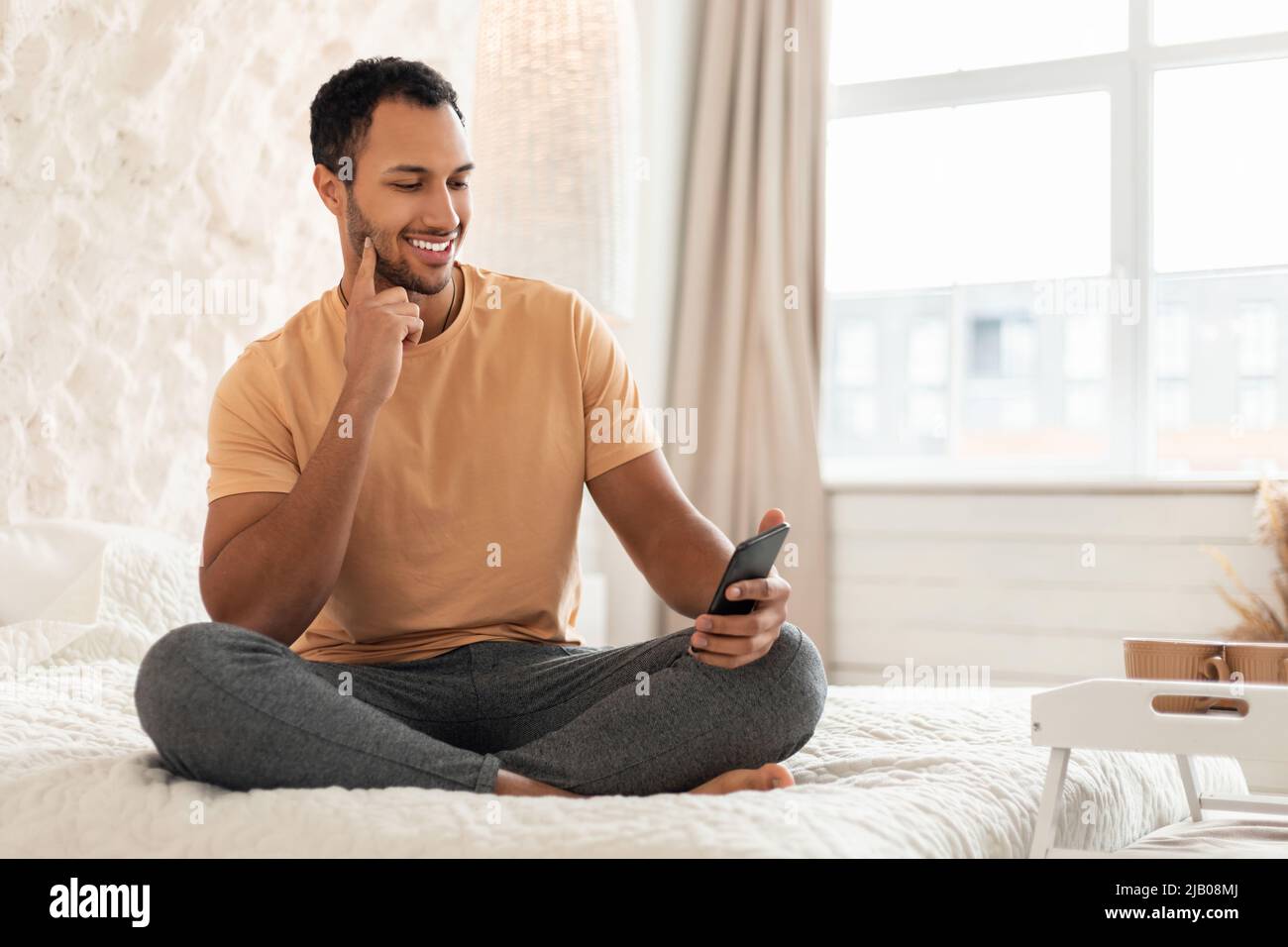 Happy Arabic Male Texting Using Phone Sitting In Modern Bedroom Stock ...