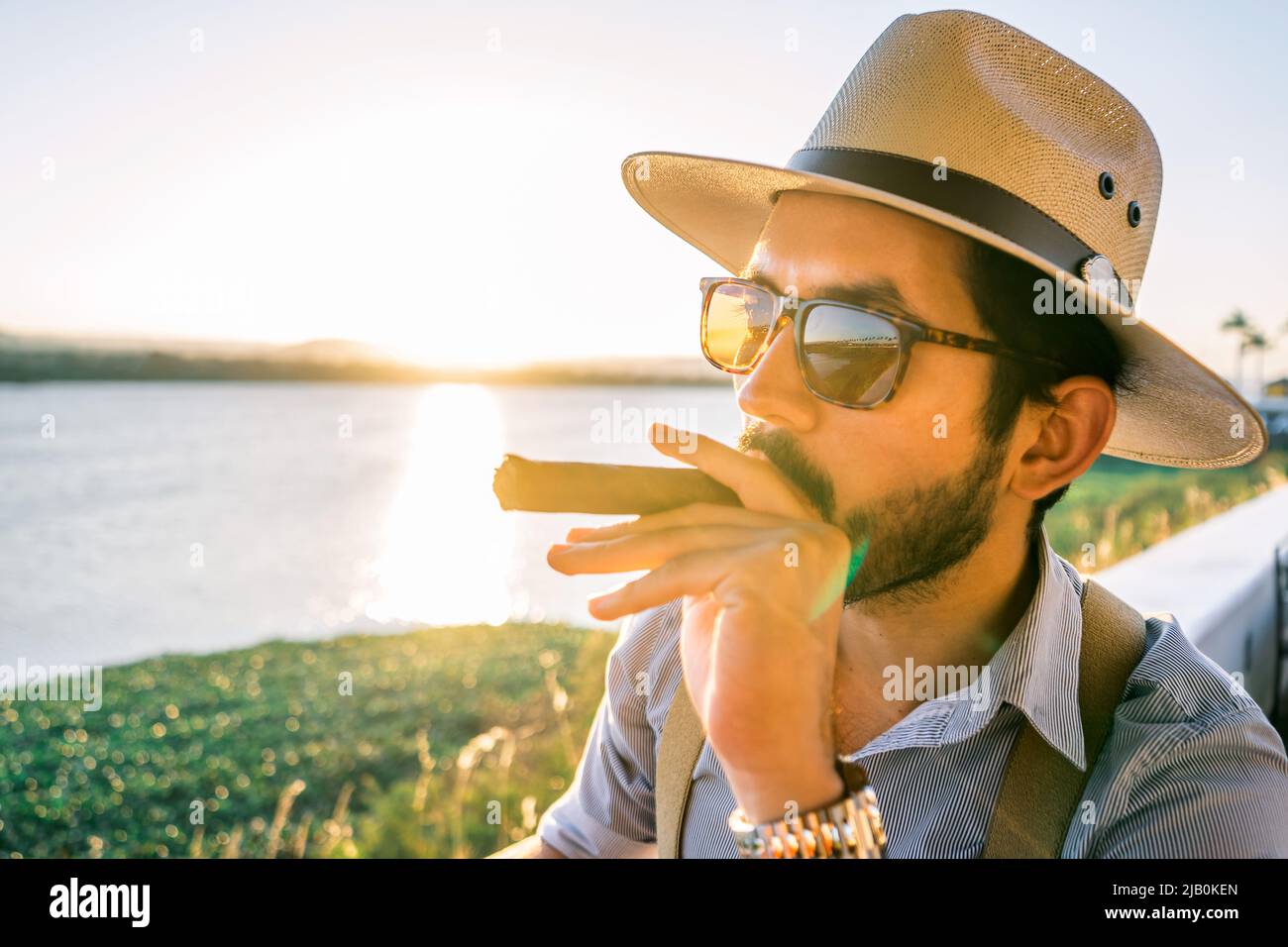 Latin young man wearing glasses, hat and suspenders smoking a cigar in ...