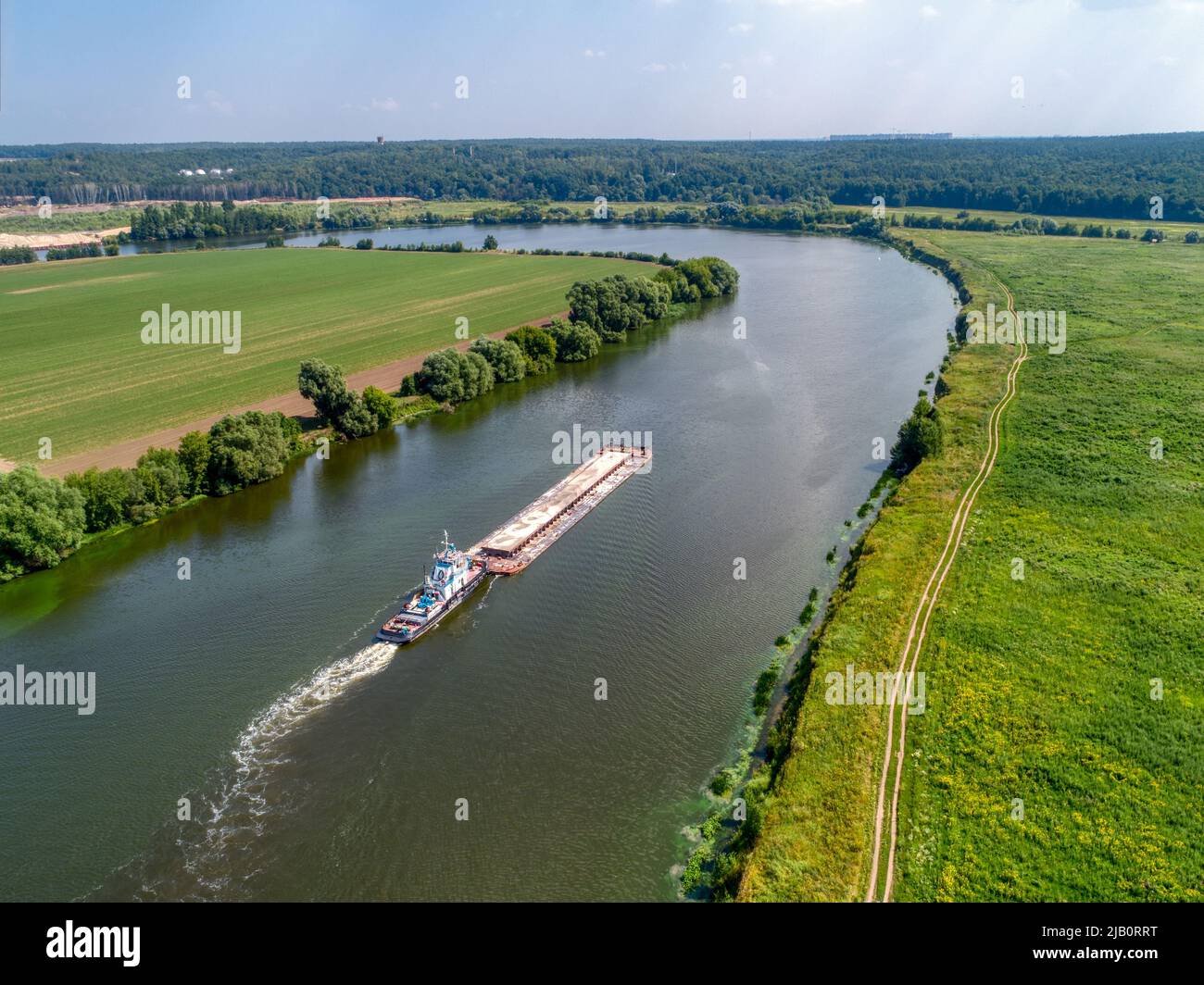 Small towboat pushes barge along calm water past fields Stock Photo - Alamy