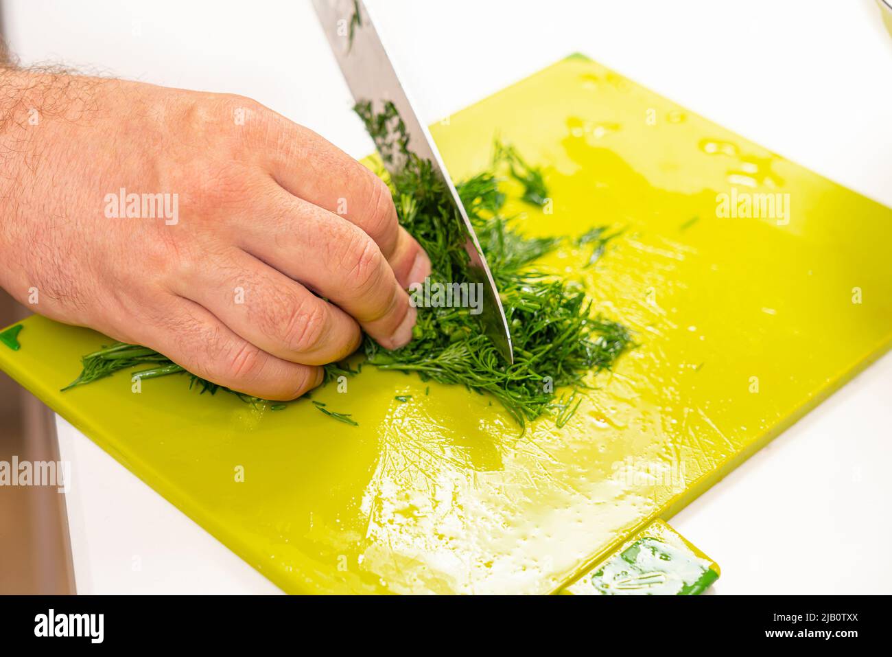 cutting dill with a kitchen knife male hands on a plastic cutting board ...