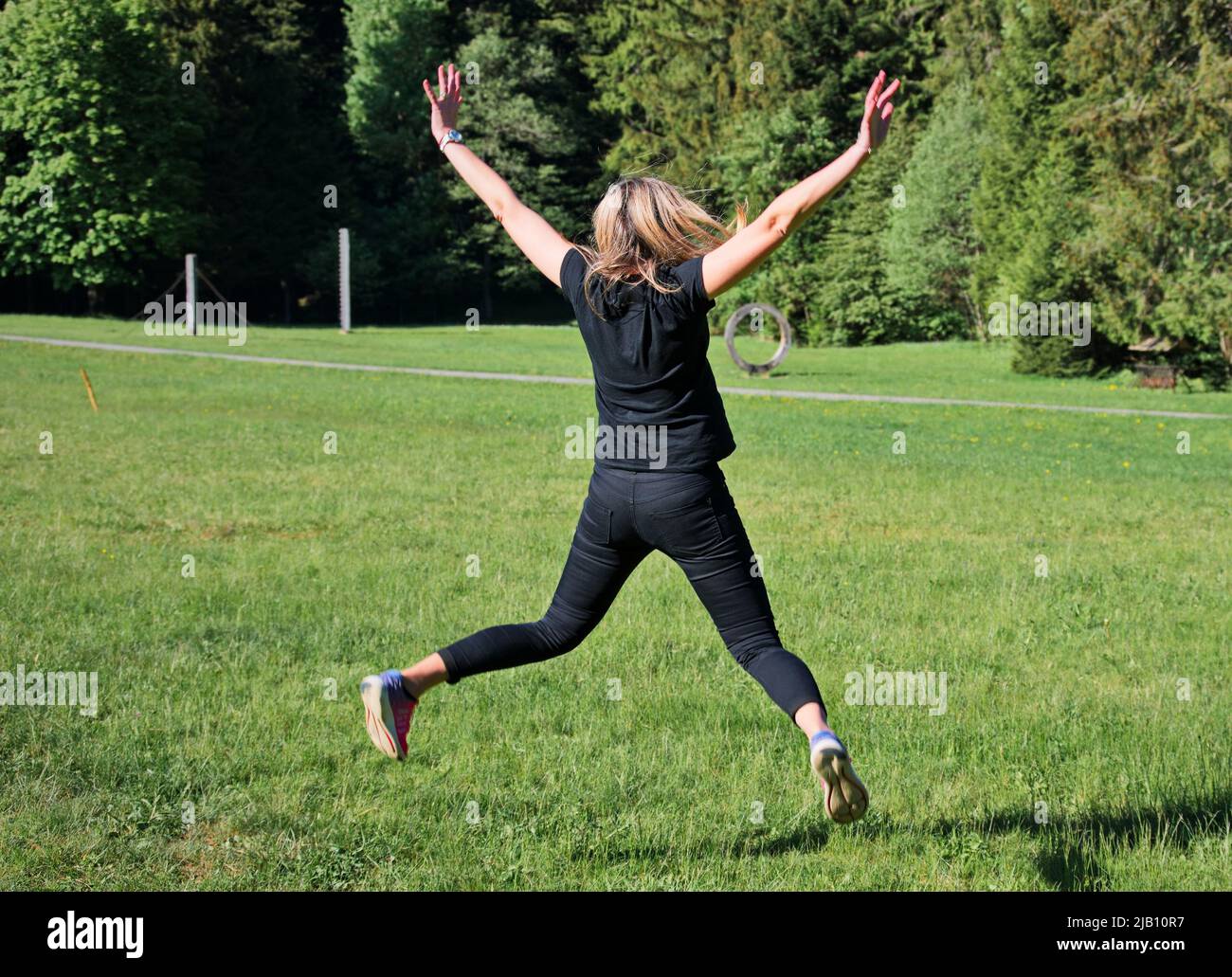 Rear view of blond woman jumping in a field Stock Photo - Alamy