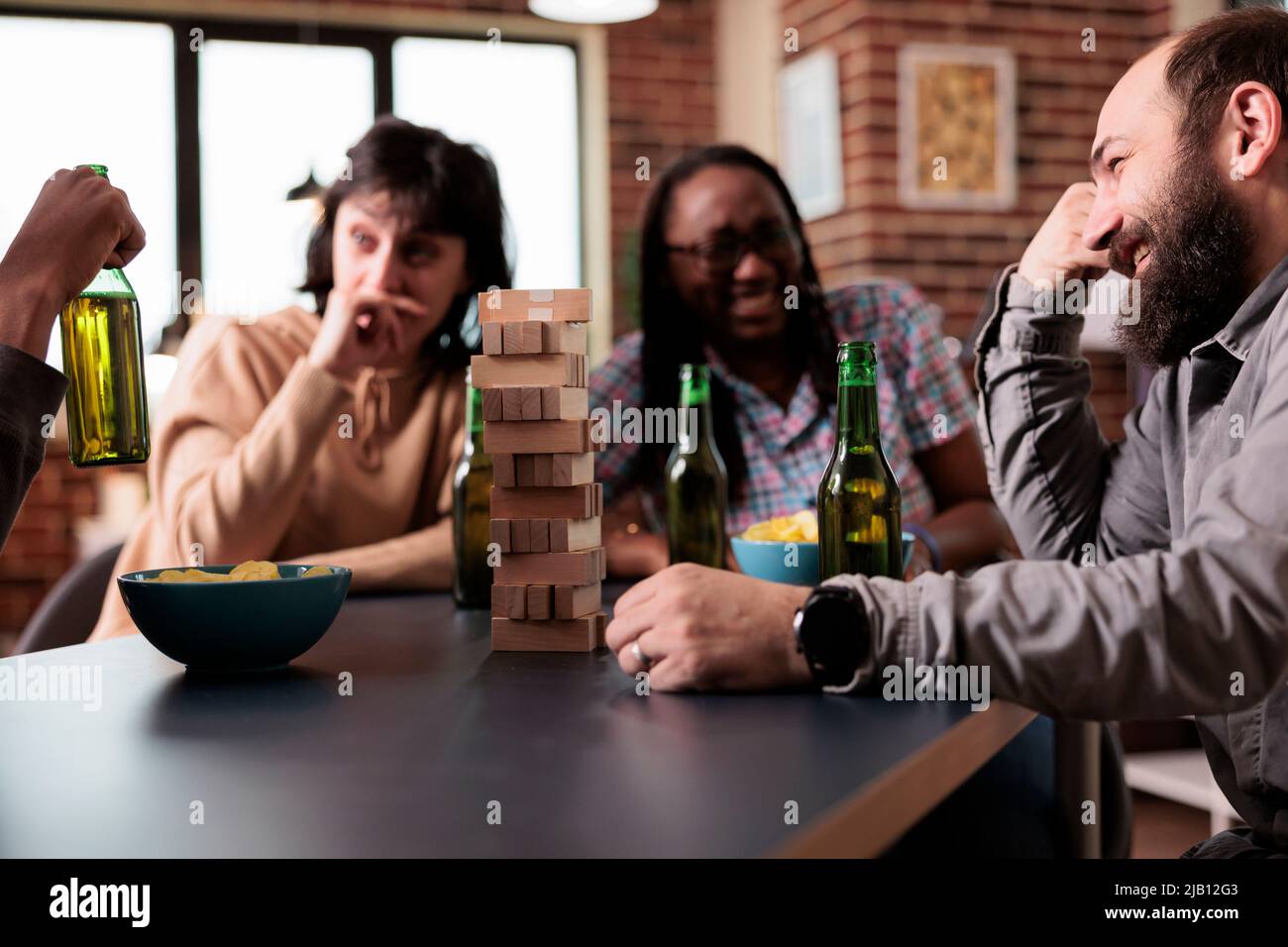 Multiethnic happy friends sitting at table in living room while playing ...