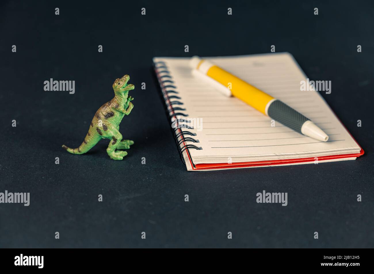 A pen, a spring-loaded notebook, and a miniature dinosaur against a ...