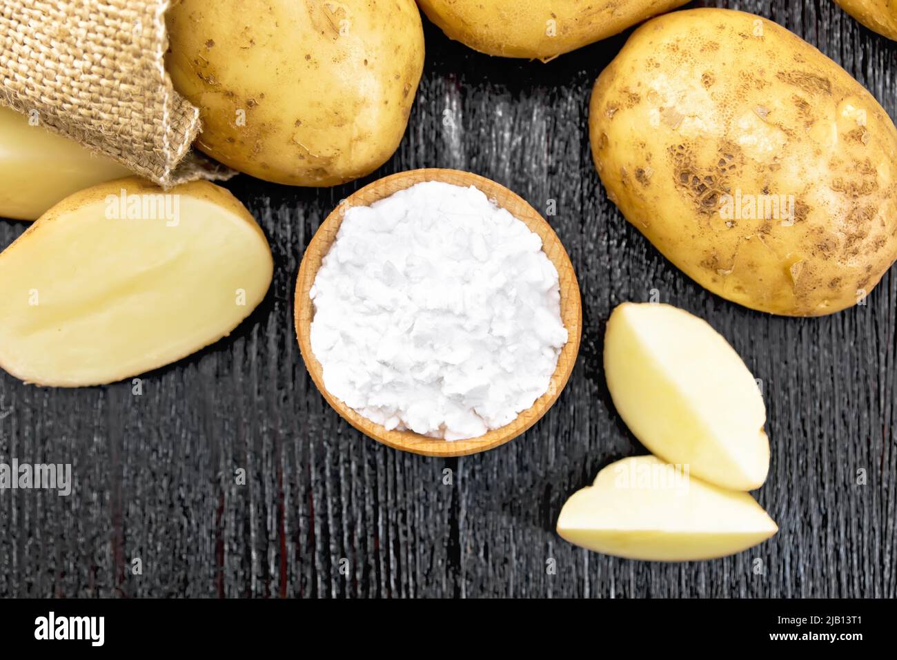 Potato starch in bowl, vegetable tubers in a bag and on a table against ...