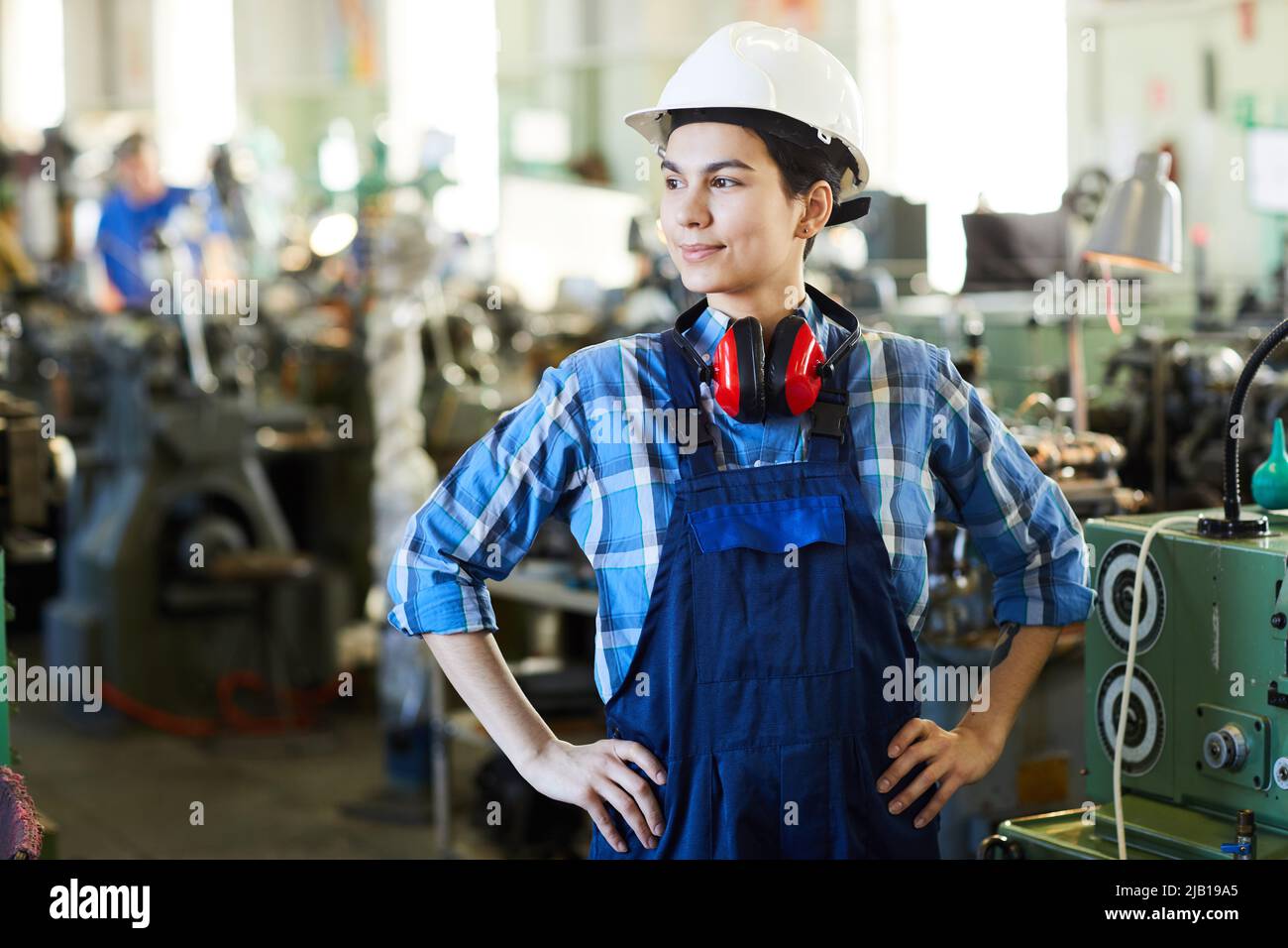 Content purposeful skilled female factory worker with ear protectors on ...