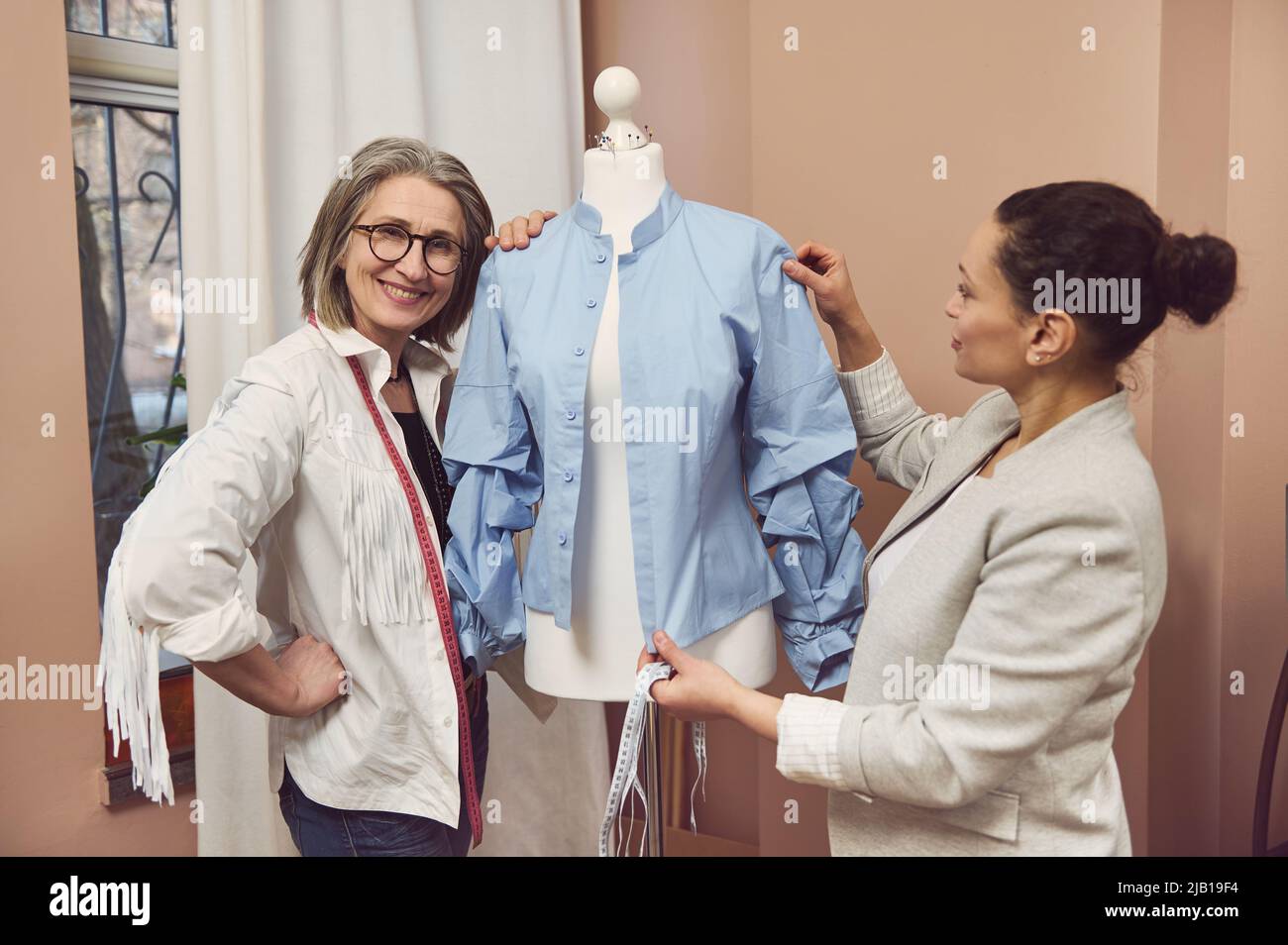 Senior fashion designer smiles posing with a dressmaker model wearing a ...
