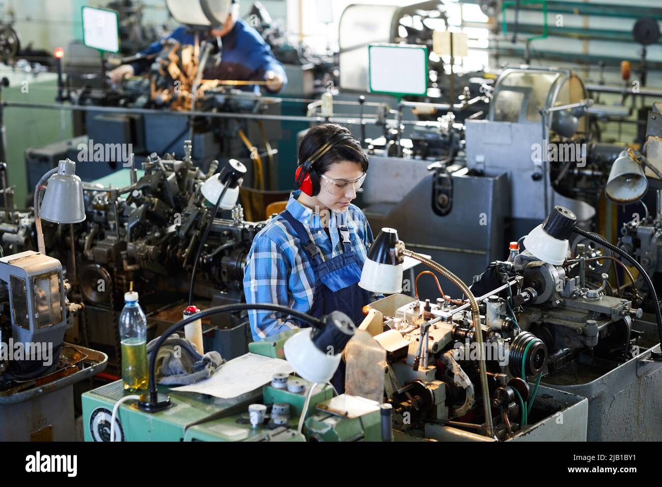 Serious busy pretty girl looking like boy standing at workbench with ...