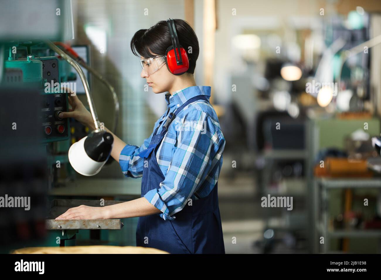 Serious skilled woman machinist in ear protectors and safety goggles ...
