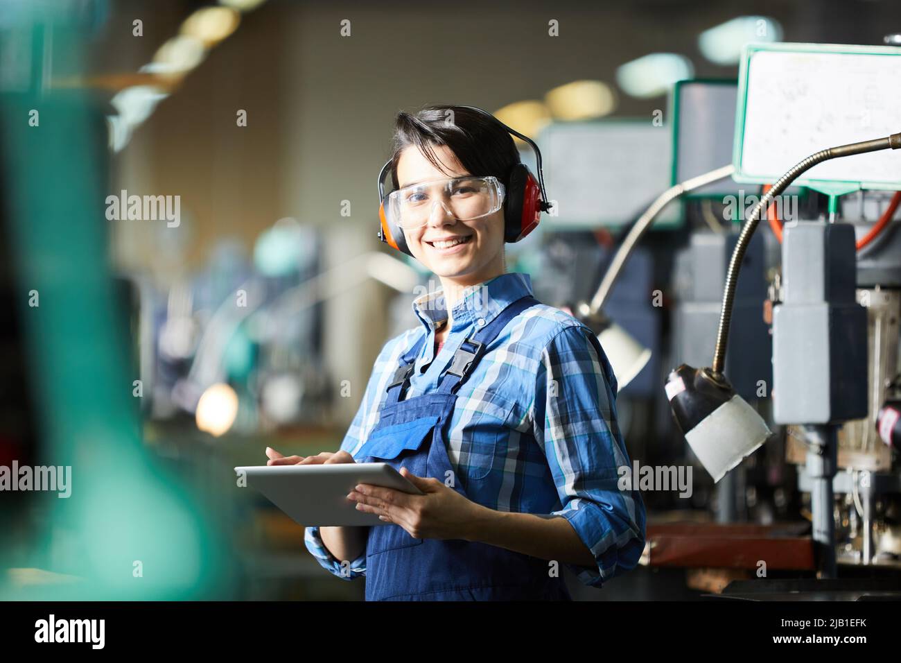 Smiling excited young female technician in protective goggles and ear ...