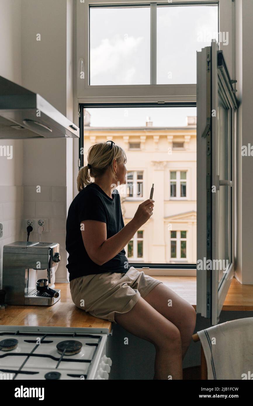 Mature woman smoking e cigarette at home near the window. Caucasian 40 ...