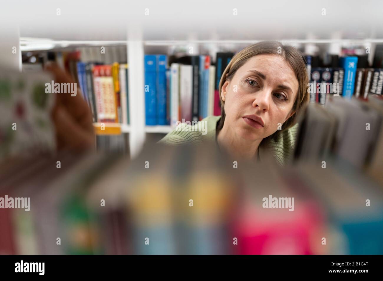 Middle-aged female choose book from bookshelf in college, university library for education ...