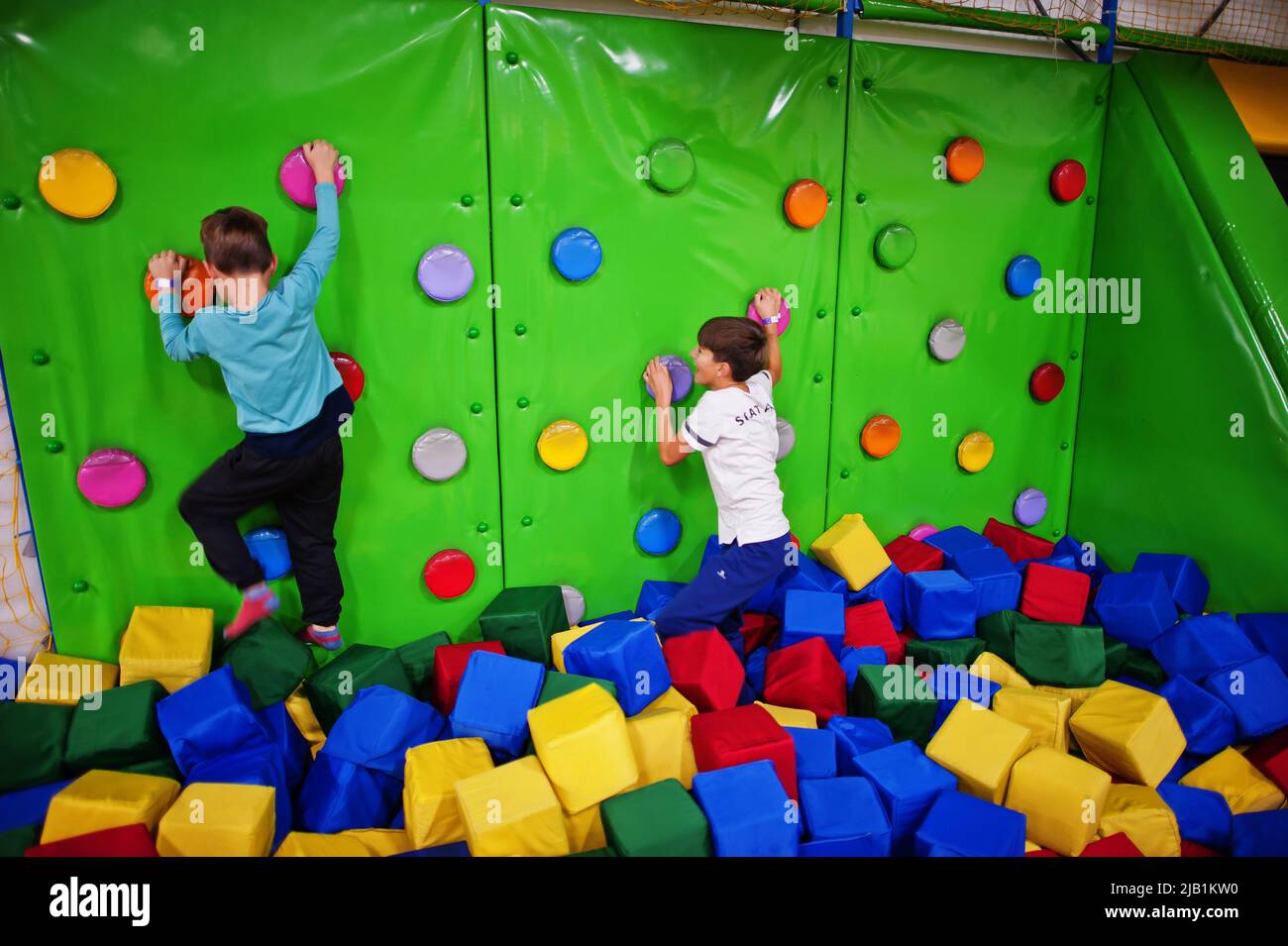Two brothers kids climbing on a green wall in attraction playground ...