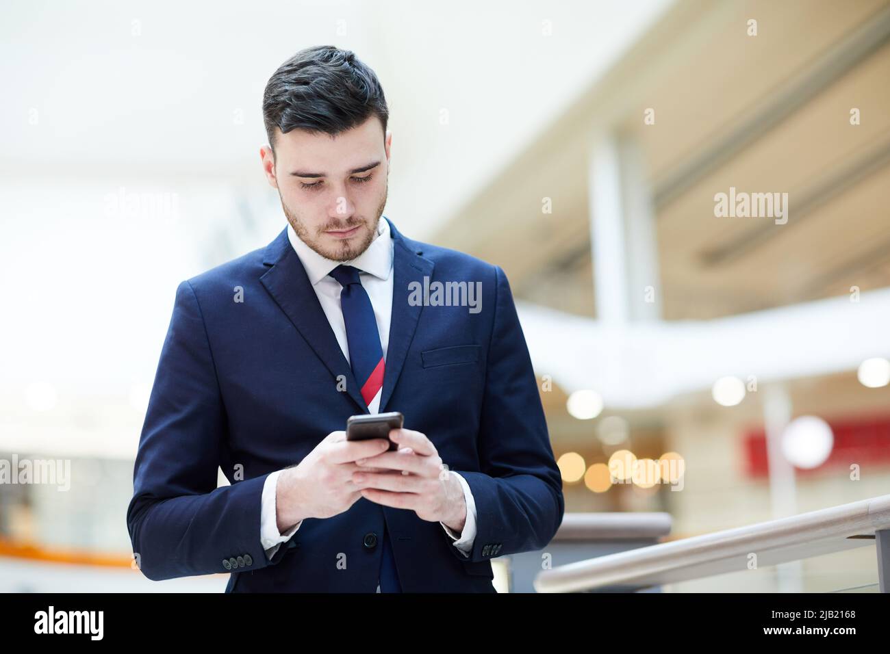 Serious busy young male manager in formal suit standing in lobby and ...