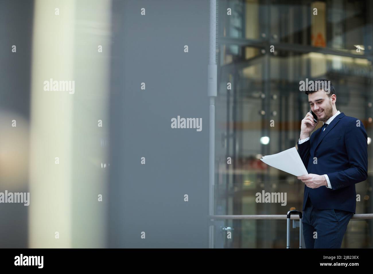 Positive handsome young male manager in suit talking by mobile phone ...