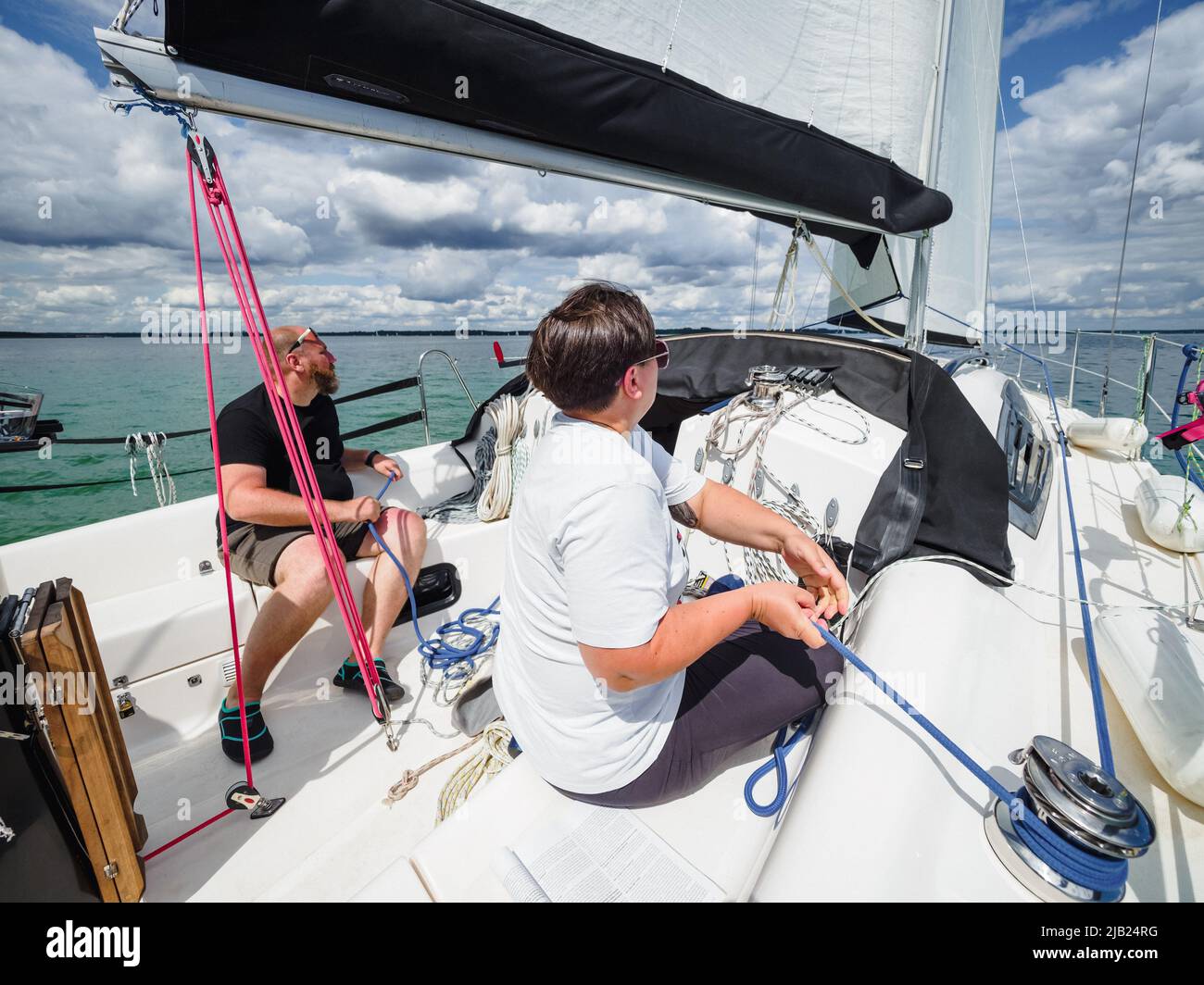 couple sailing on a yacht. adult man and woman using a winch to pull a ...