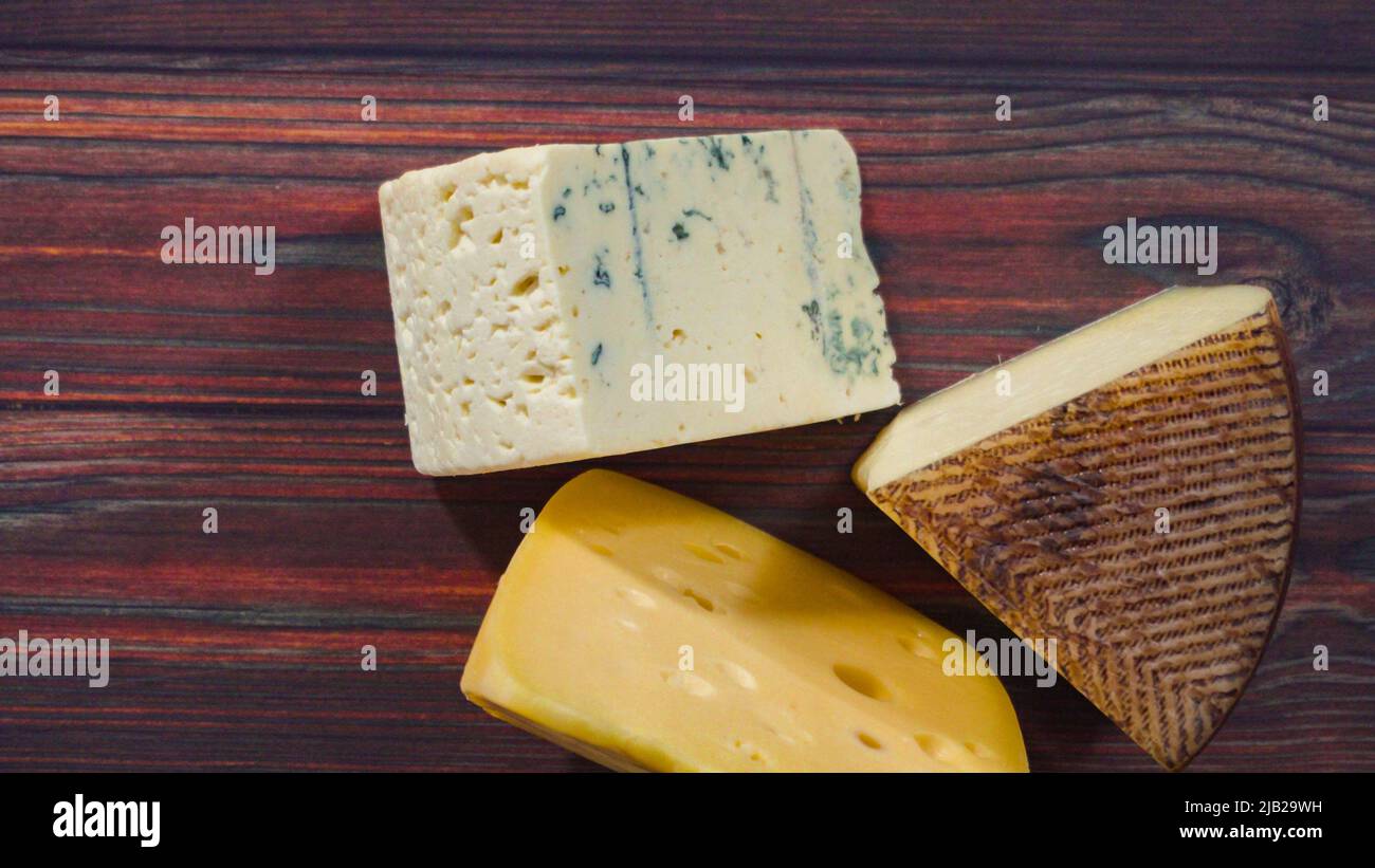 Flat lay. Large wedges of gourmet cheese on a rustic wood background ...