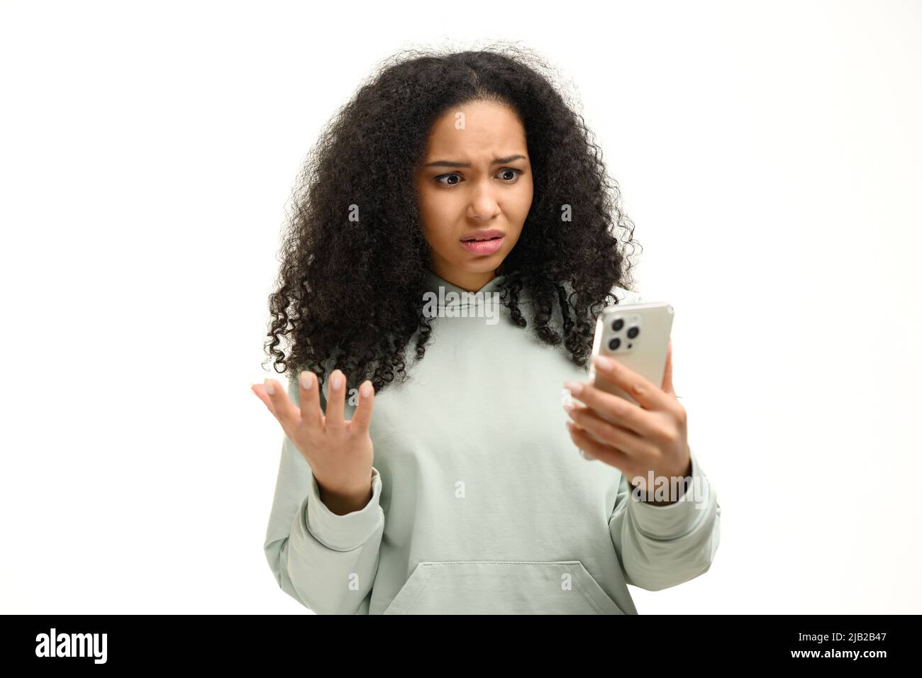 Disappointed young African-American woman holding smartphone and ...