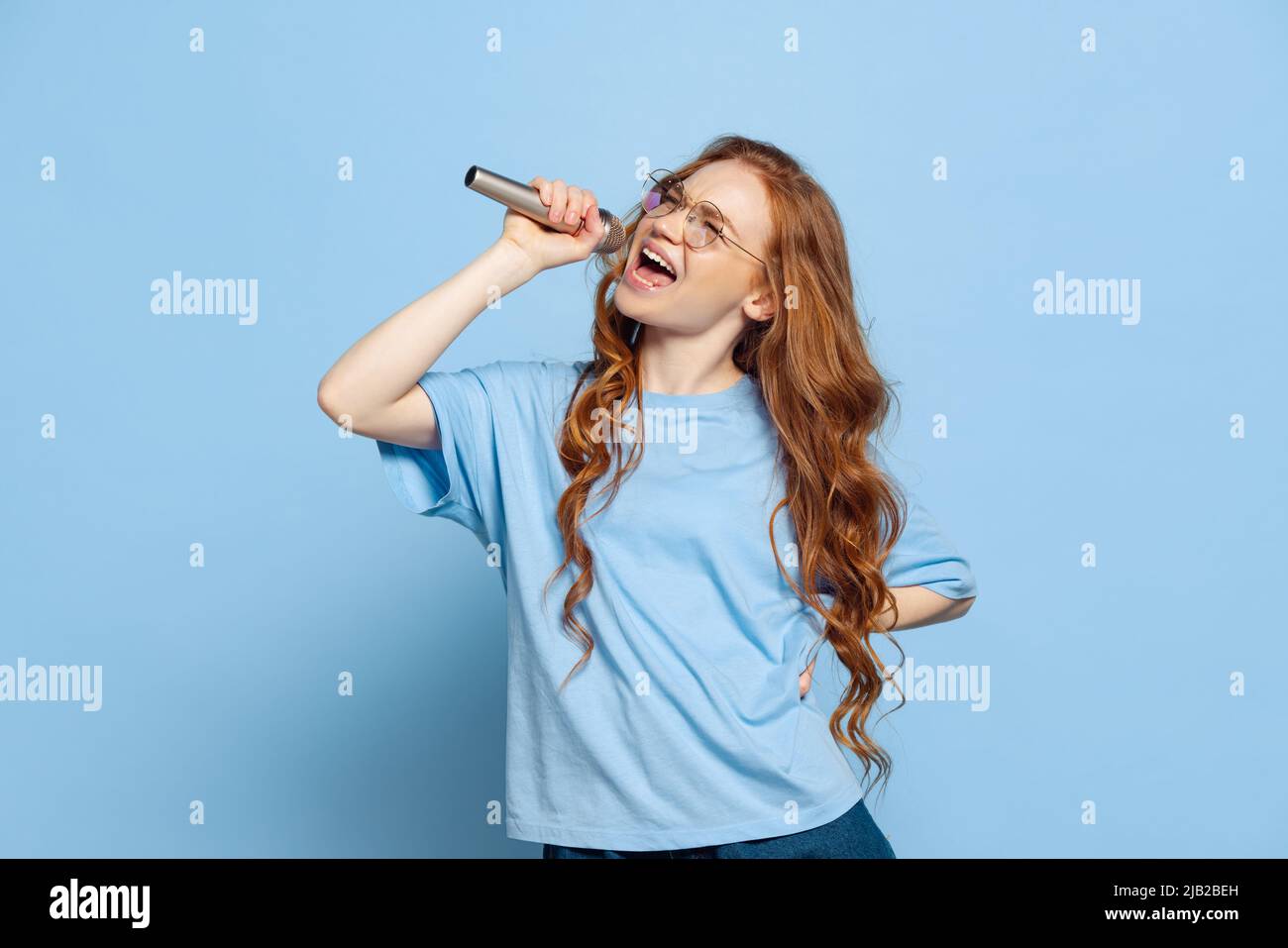 Studio shot of excited young redhead girl, student singing isolated on ...