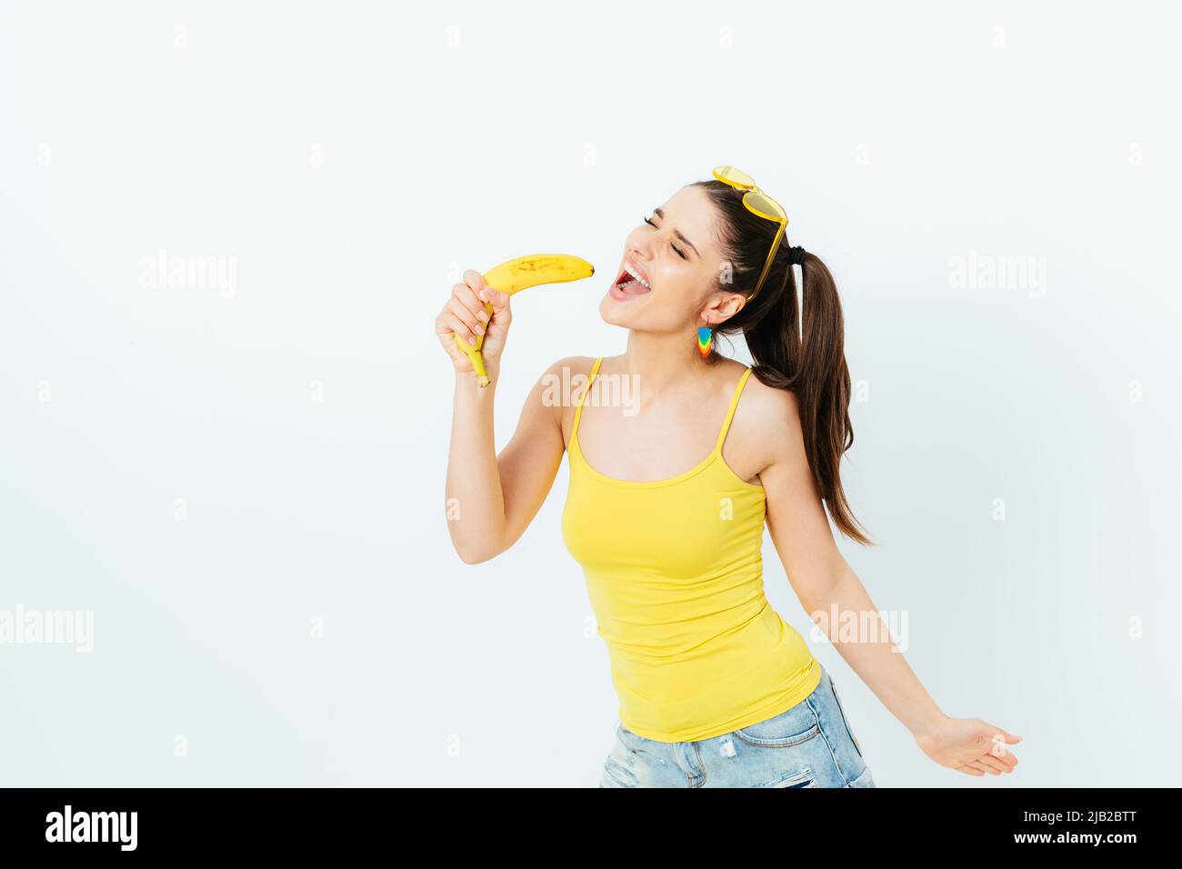 Cheerful young woman wearing summer outfit singing using banana as ...