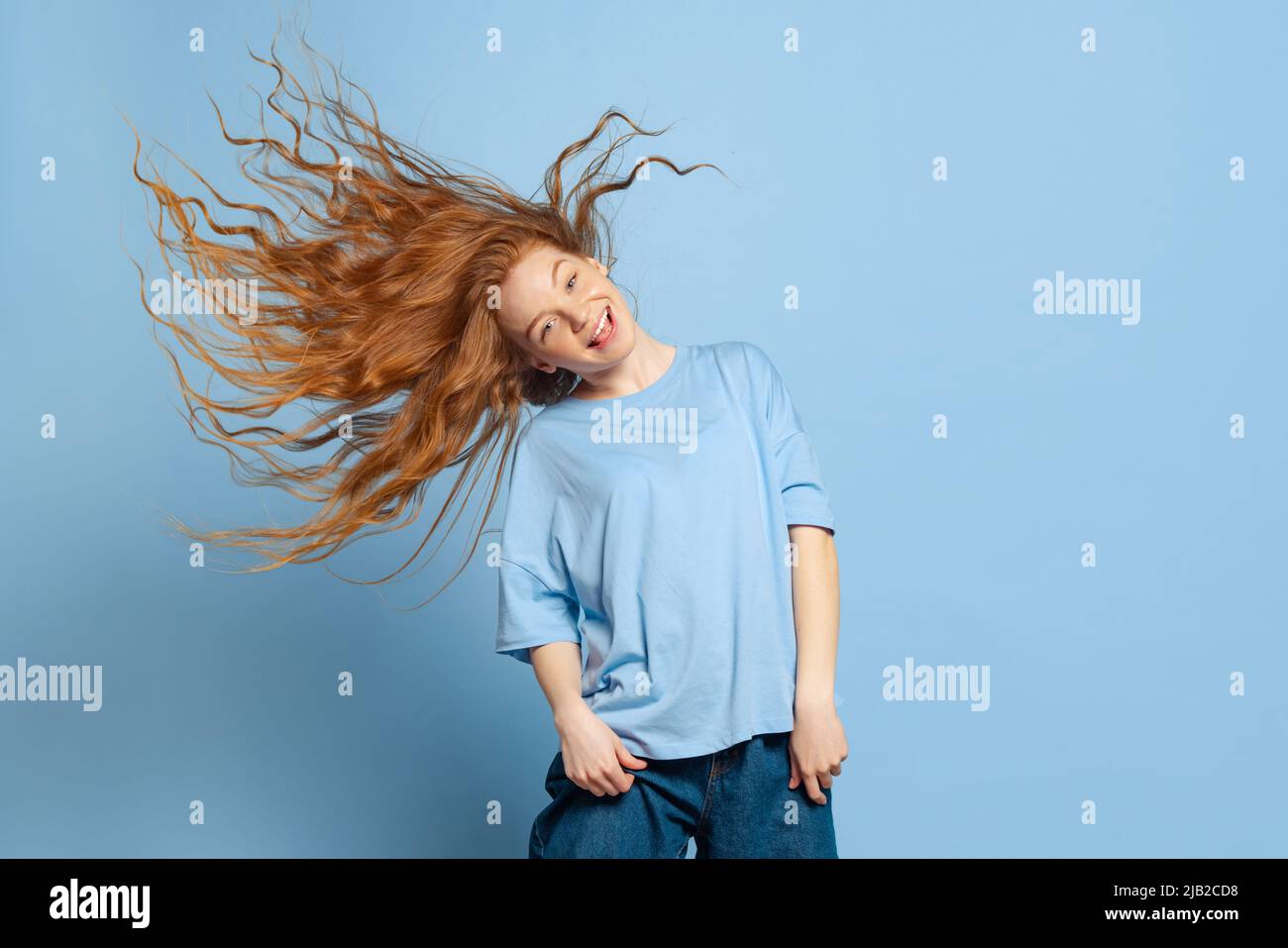 Emotional young redhead girl, student shaking her head isolated on blue ...