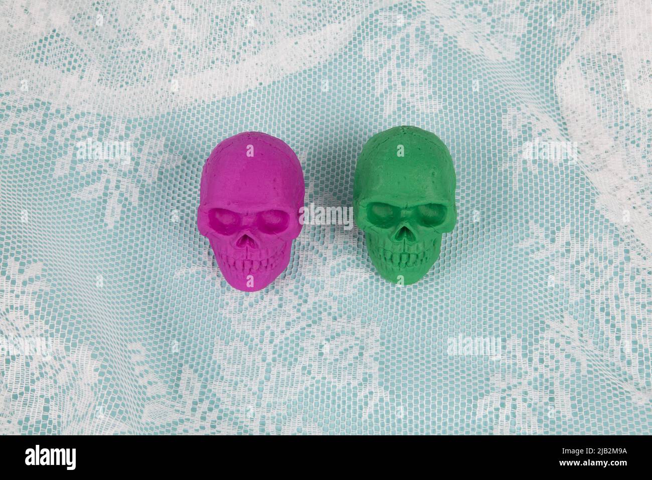 Two plastic skulls, one pink and one green, placed on a lace curtain ...