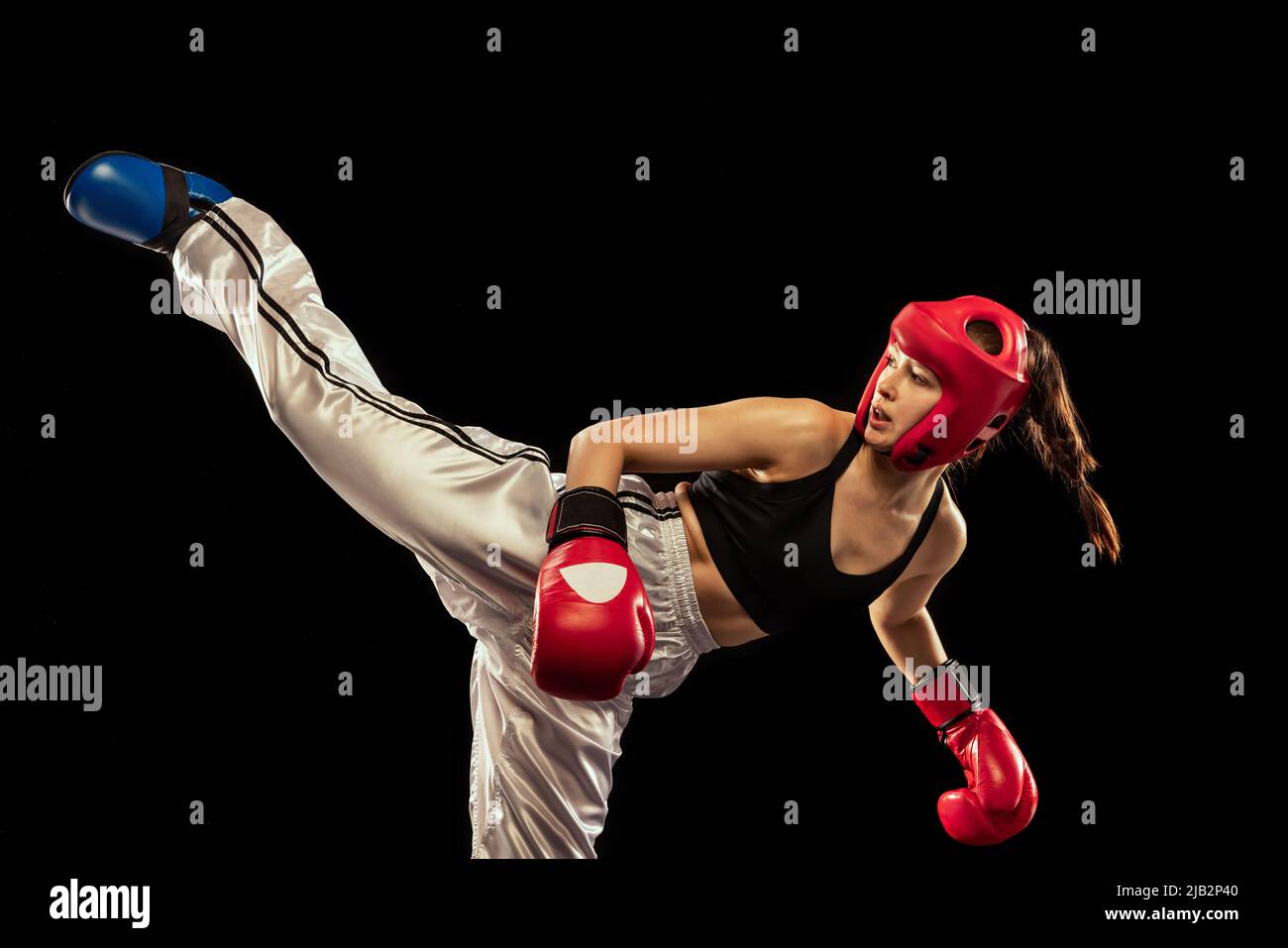 High kick. Attractive female boxer in boxing gloves and helmet training ...