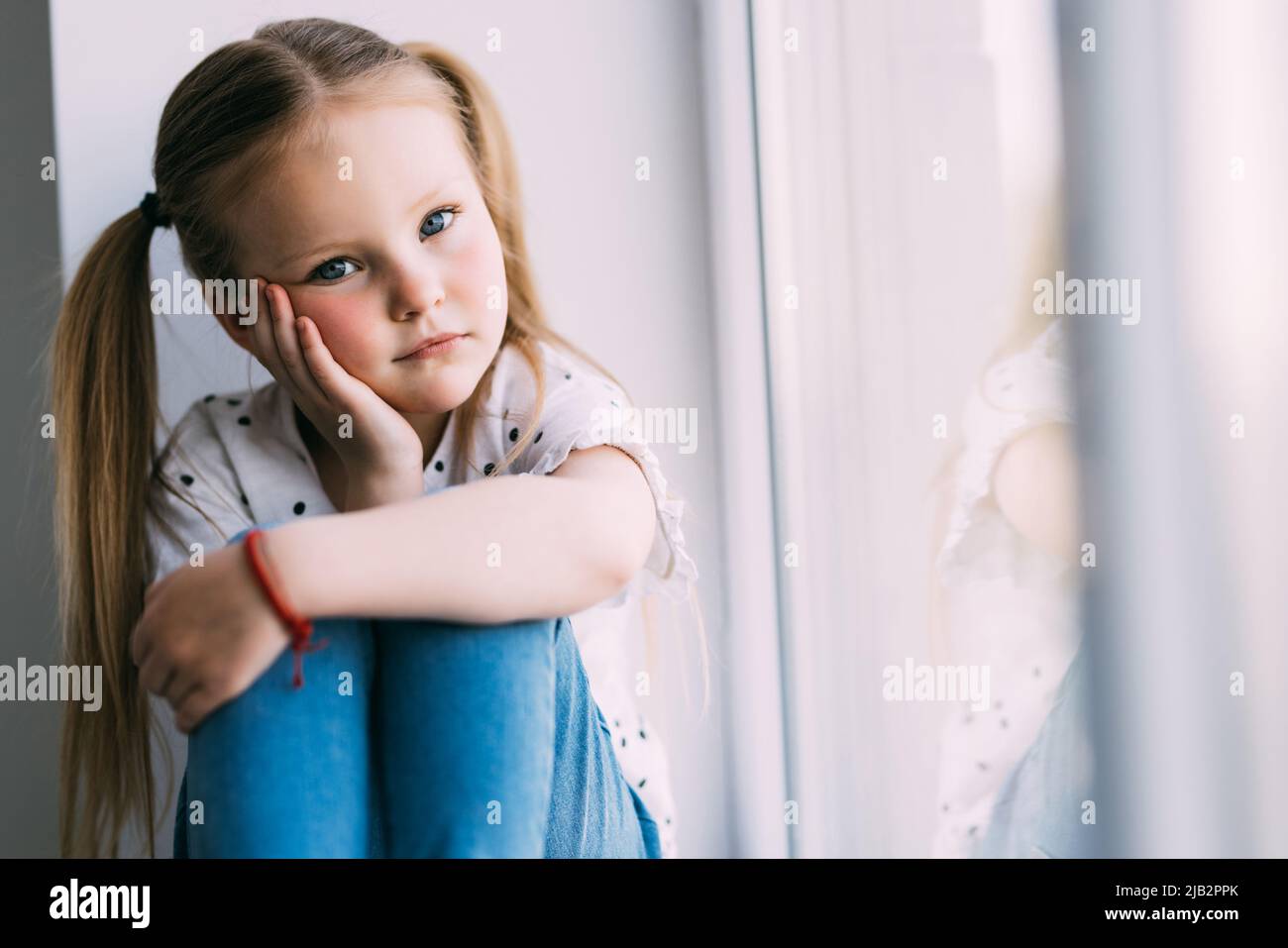 Little sad girl sitting on windowsill Stock Photo - Alamy