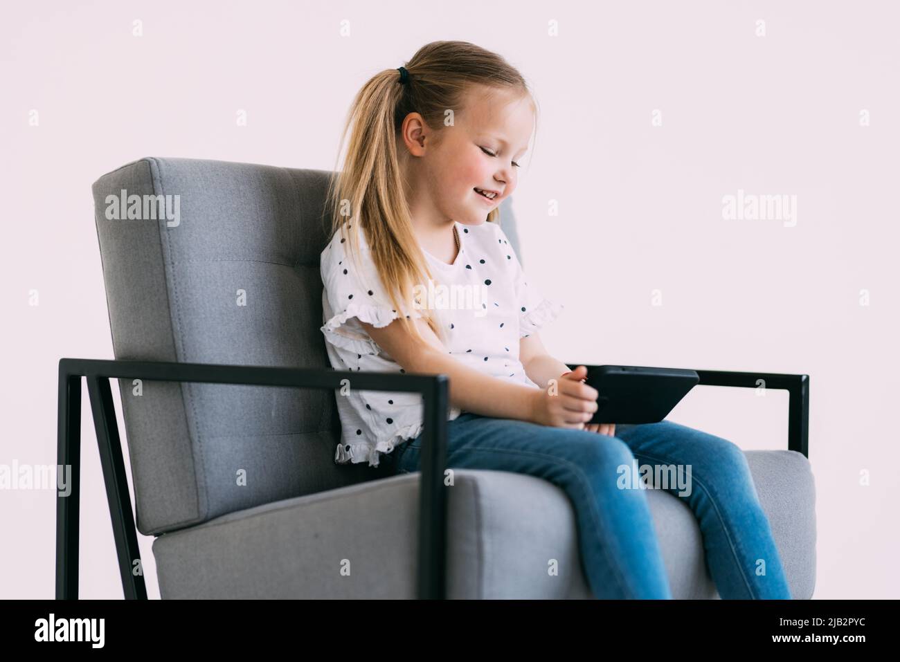 beautiful concentrated schoolgirl sitting on chair and using smartphone isolated on white Stock ...