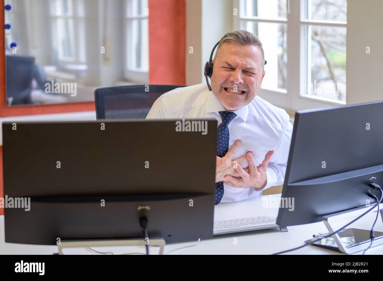 Businessman suffering a heart attack at work in the office clutching at ...