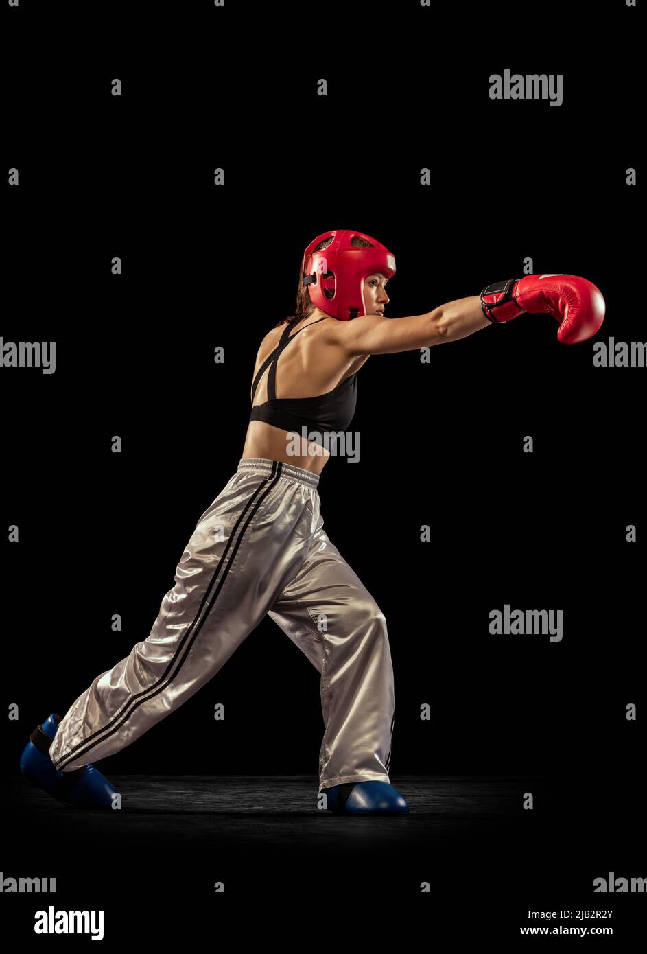 Young female boxer in boxing gloves and helmet training isolated on ...