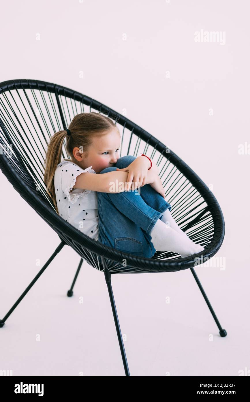 Portrait of little sad girl sitting on chair isolated over white ...