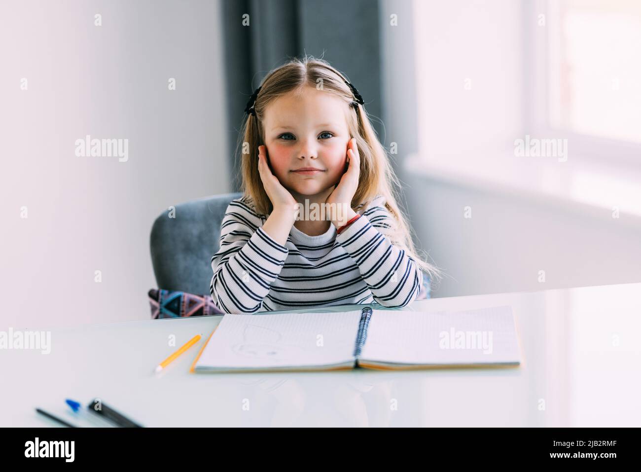 Unhappy little Caucasian girl child sit at table at home feel lazy ...