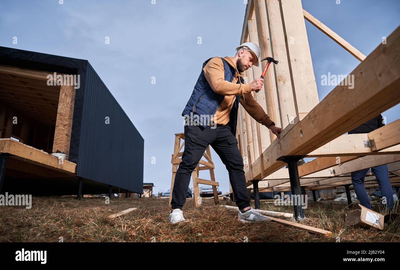 Man worker building wooden frame house on pile foundation. Carpenter ...