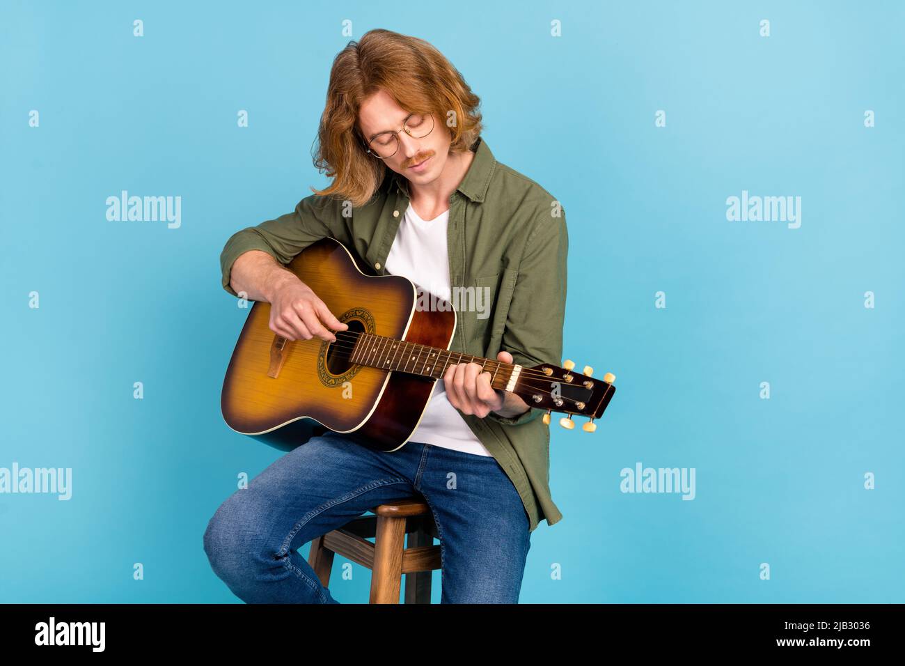 Portrait of attractive talented guy sitting on stool playing string ...