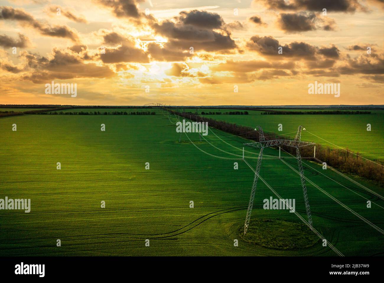 Power line in the rays of the setting sun through the green fields ...