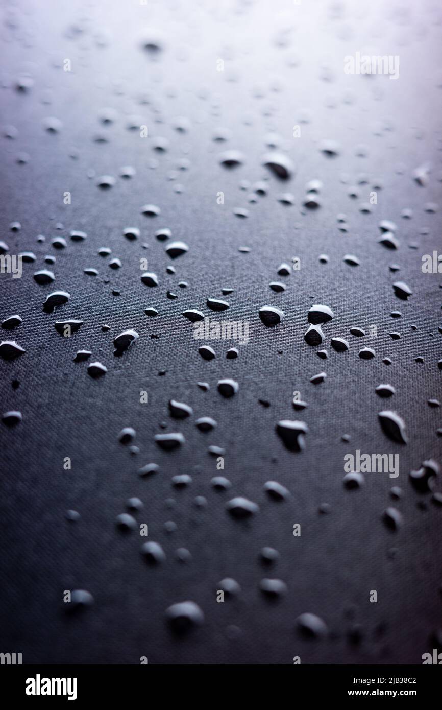 Selective focus on water drops on slippy surface of black synthetic ...