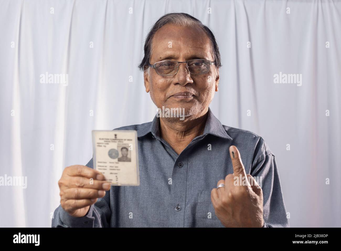An Indian old man smiling with voter card in hand on white background ...