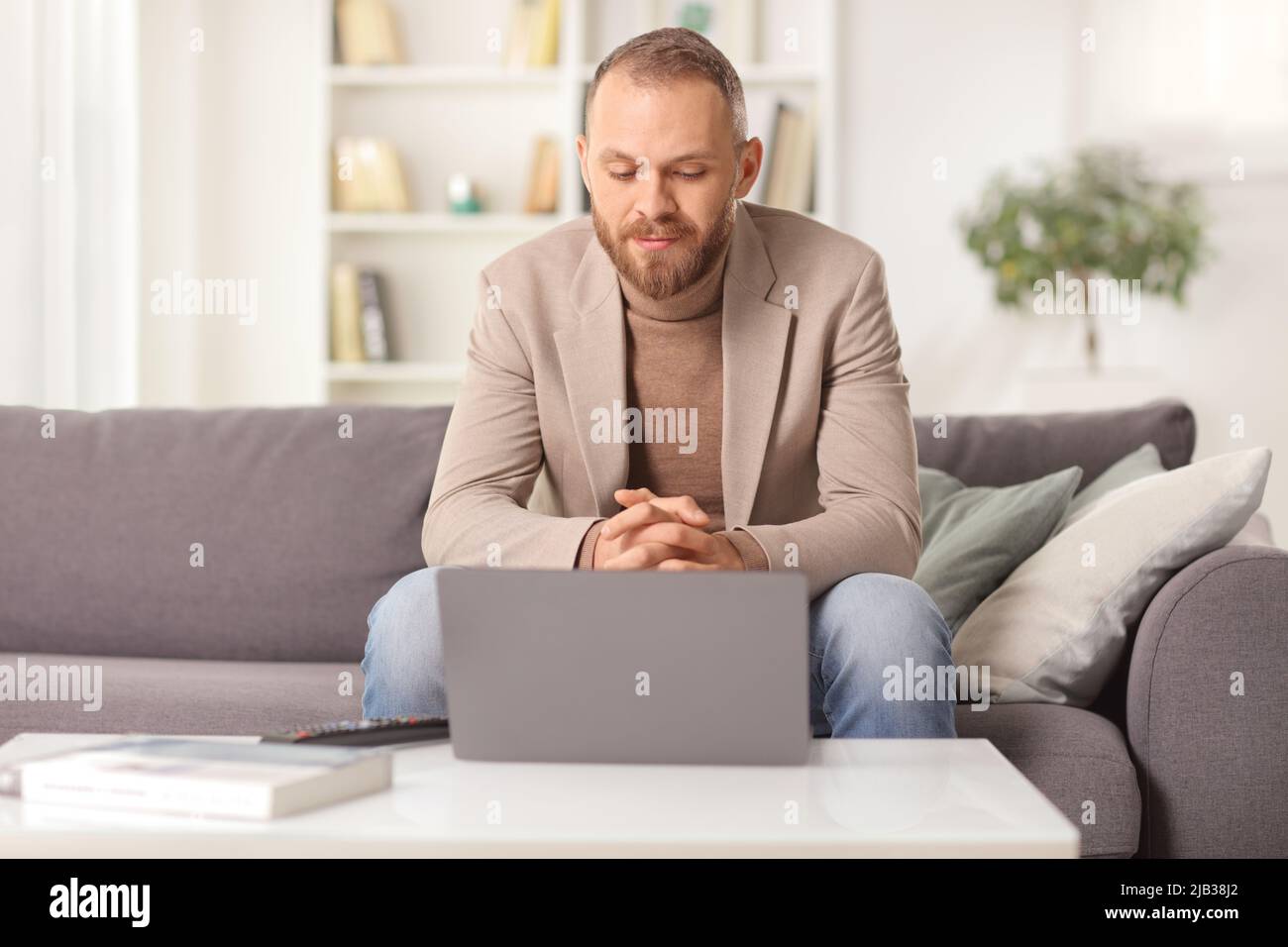 Young man sitting on a sofa at home and looking at a laptop computer ...