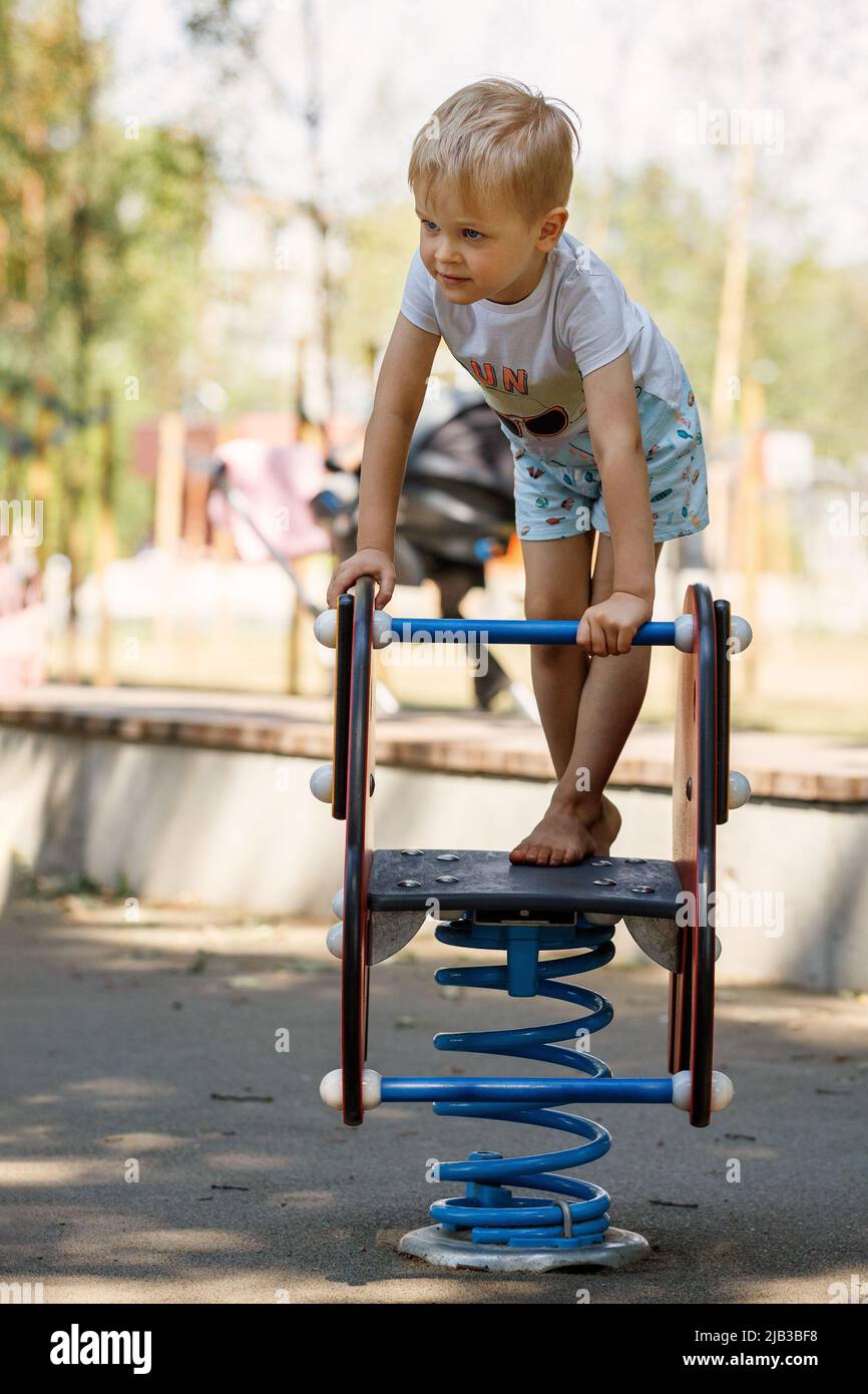 The brave little boy stands up and balances on a spring swing on the ...