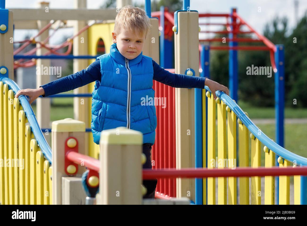 A little boy wearing a blue vest walks on a wavy bridge on a colorful ...