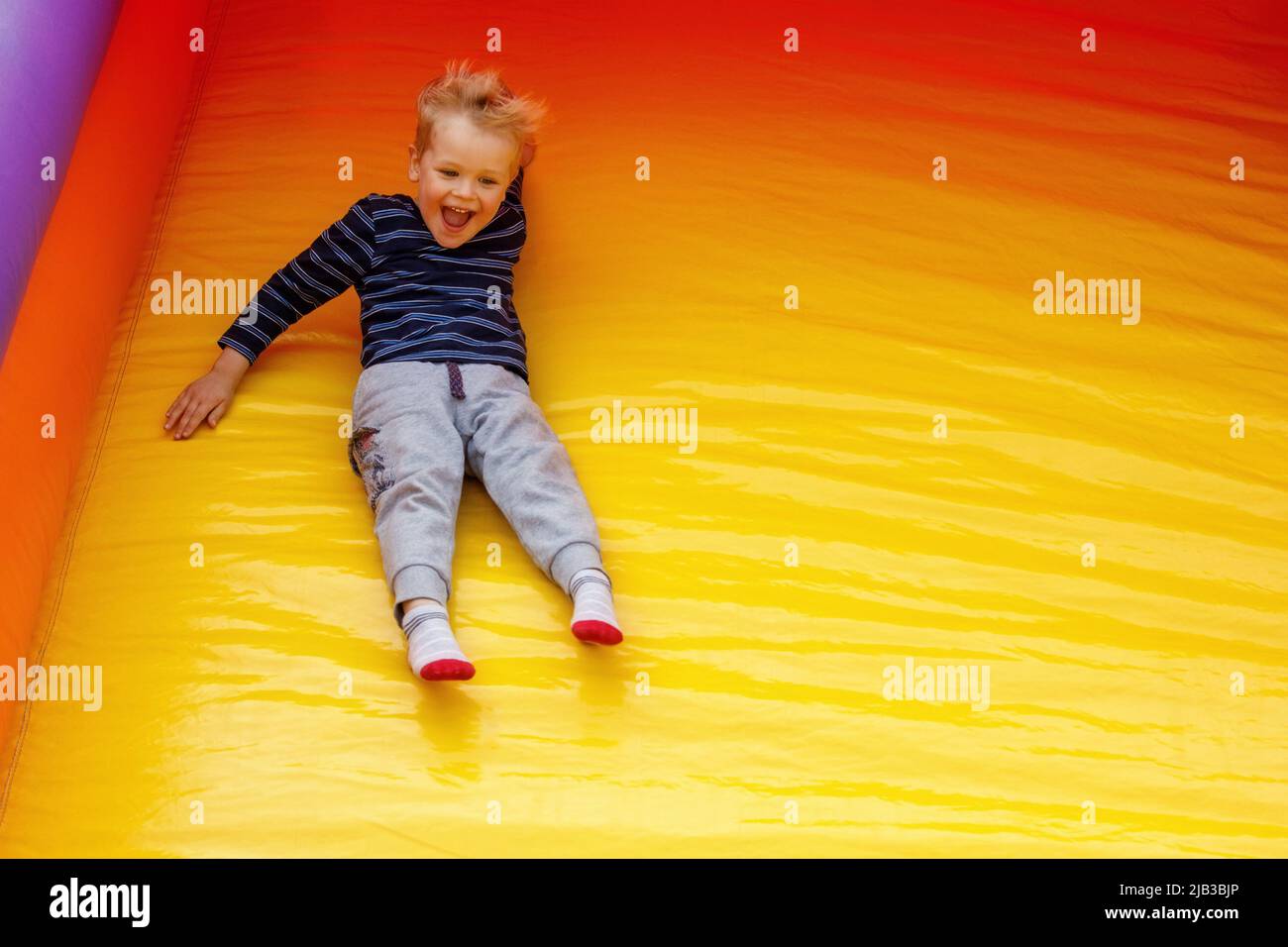 A hilarious little boy slides down at a high speed off a large, bright ...