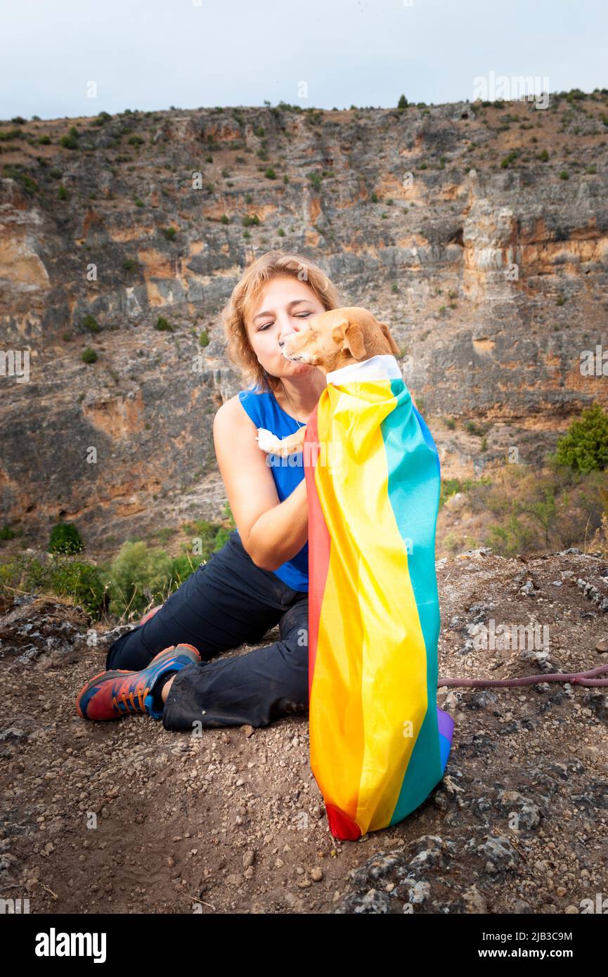 Woman on top of a cliff sitting hugging and giving a kiss to her dog ...