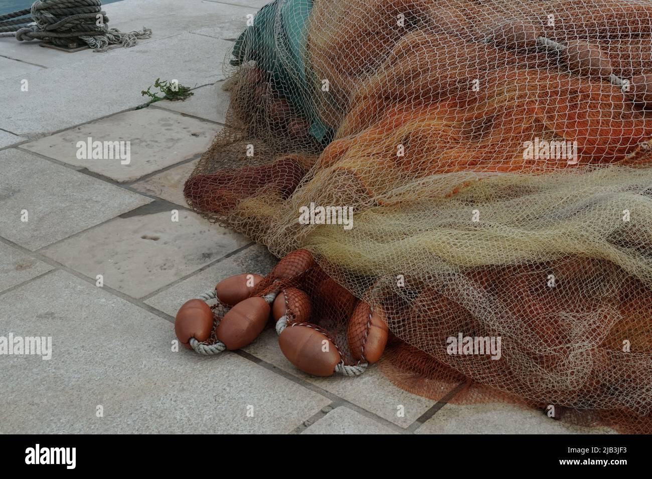 Red fishing net with red-brown floats piled on the pavement in port ...