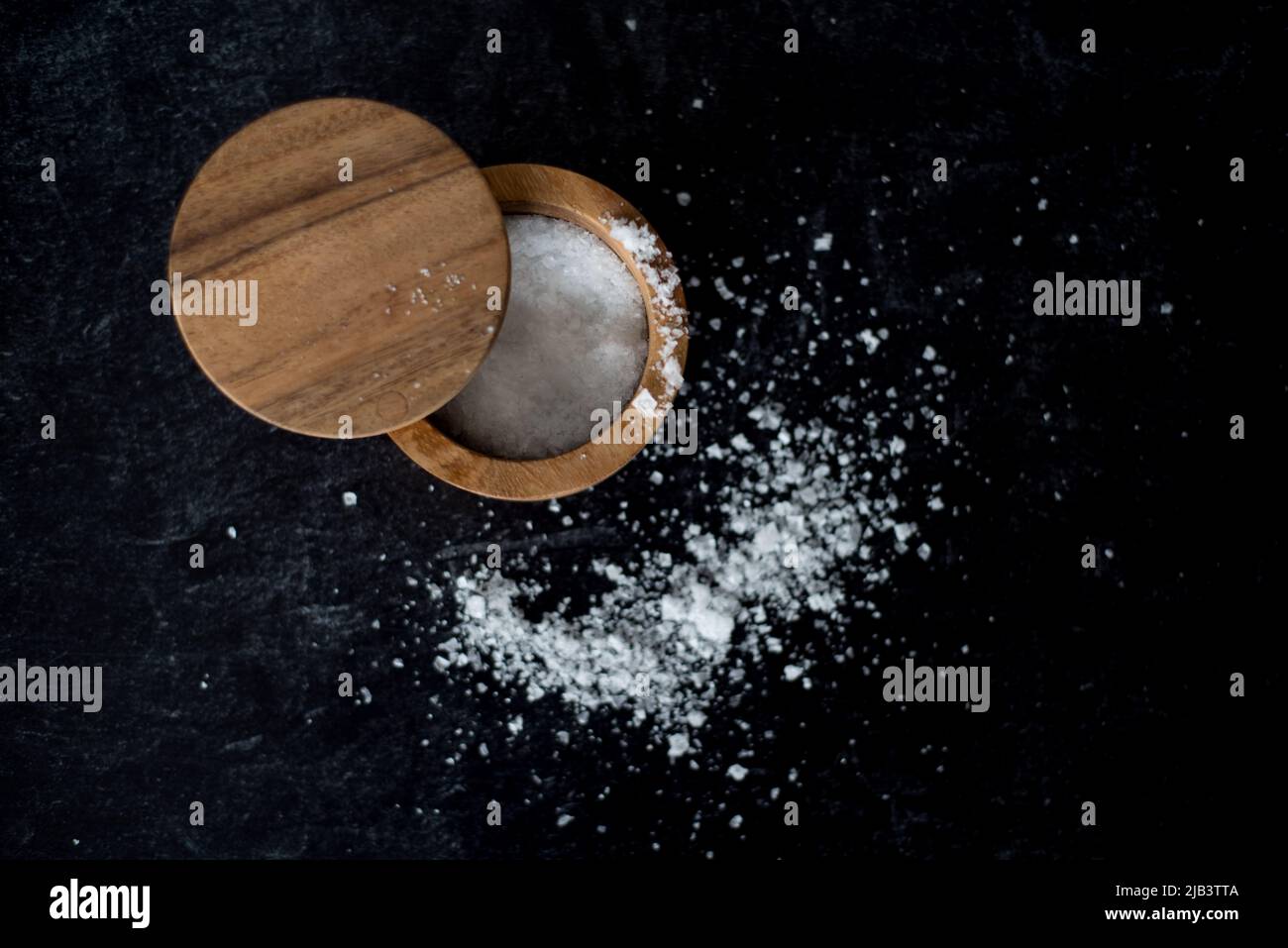 Wide top view of sea salt on dark moody background inside round wooden ...