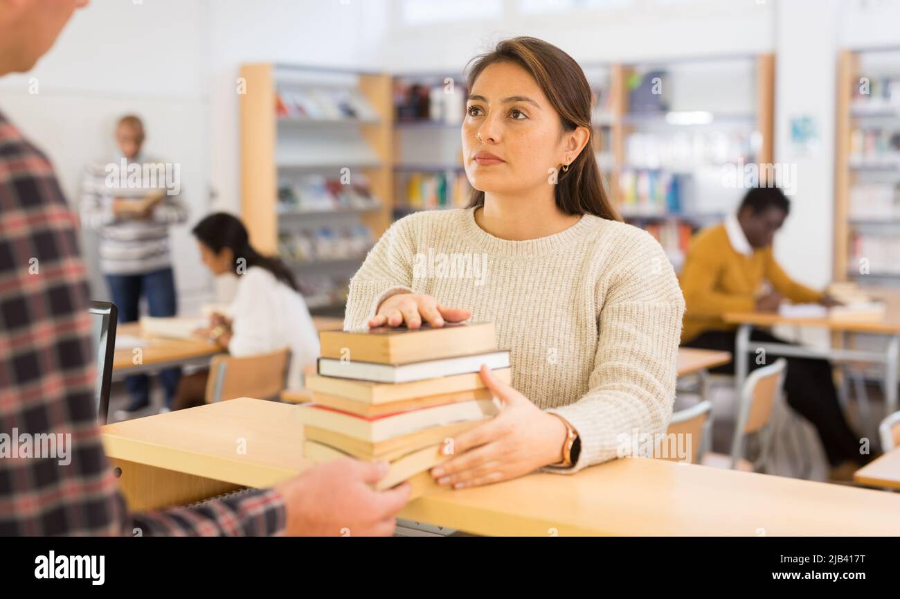 Young Latina returning books to librarian in public library Stock Photo ...