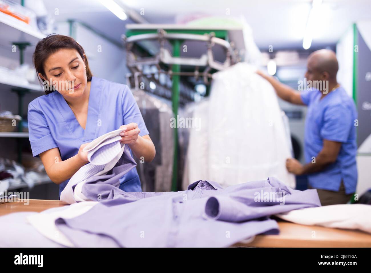 Focused woman dry-cleaning worker checking clean clothes Stock Photo ...
