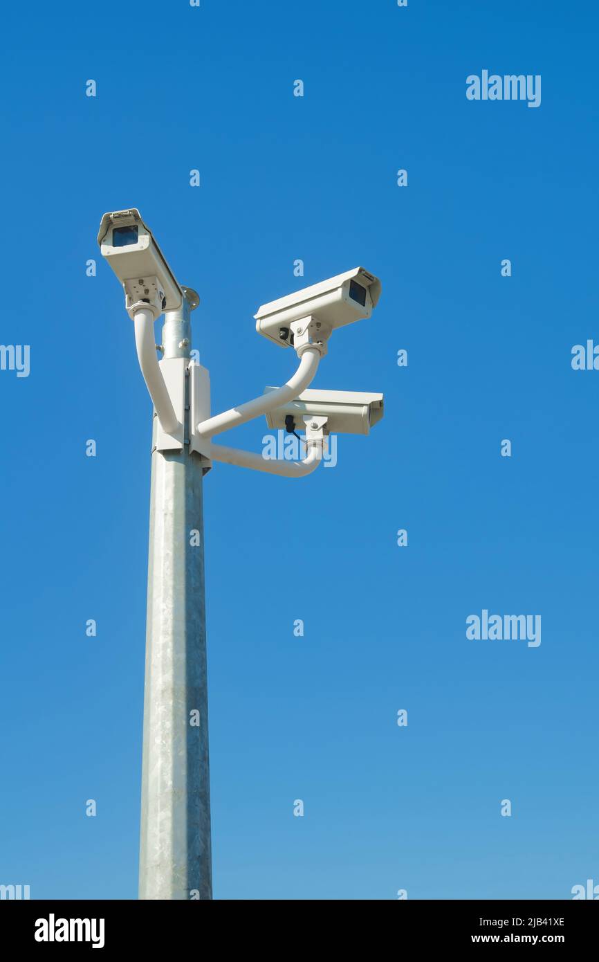 Three CCTV security cameras mounted atop a pole against a clear blue ...