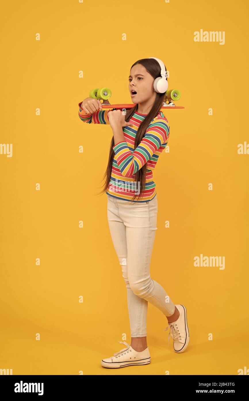serious child in headphones with penny board. teen girl listen music ...