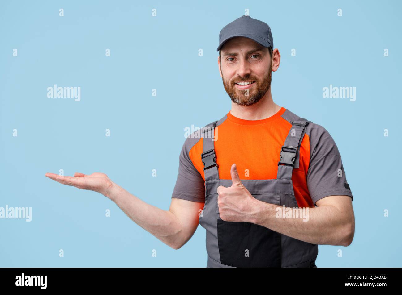 Positive worker man stands on blue background points his finger up and ...