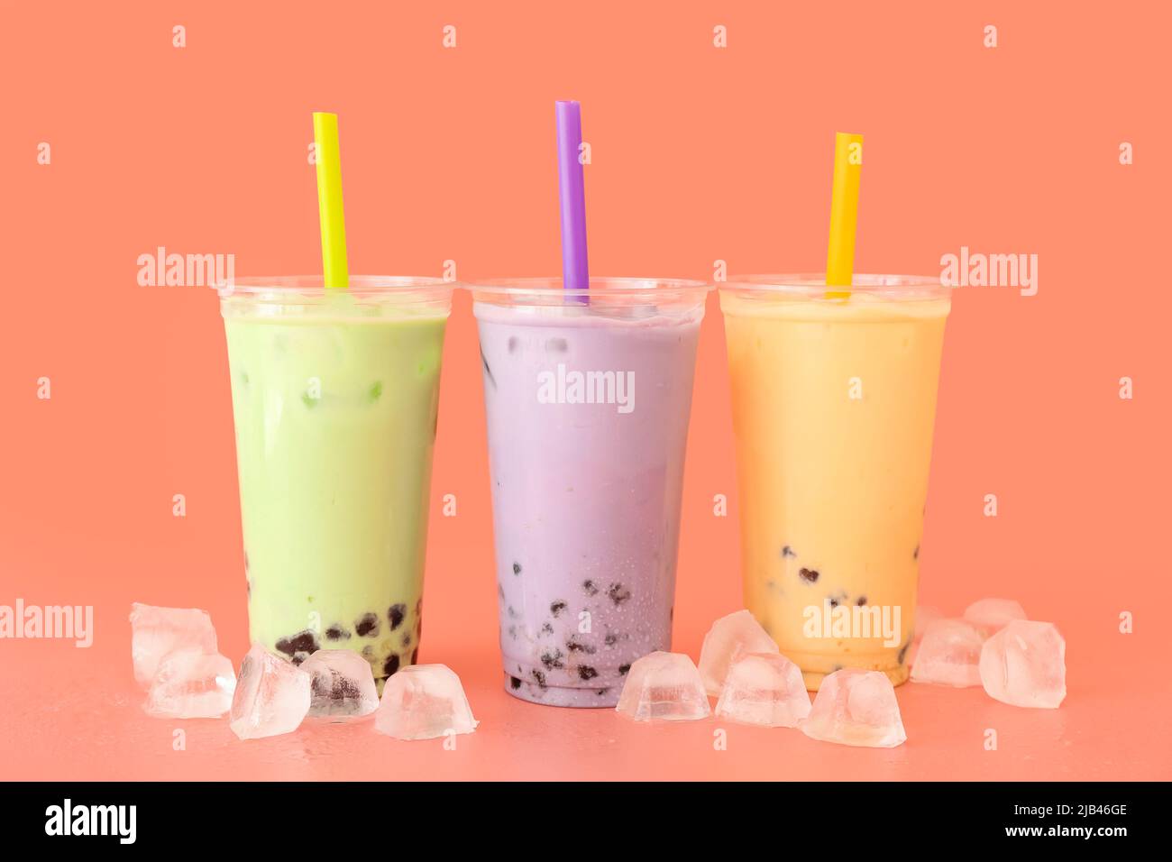 Plastic cups of tasty bubble tea and ice cubes on color background ...